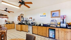 Uma área de café da manhã com armários de madeira, geladeira, espaço para café e uma placa indicando Daybreak Breakfast.