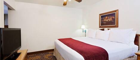 Quarto de hotel com cama, televisão, ventoinha no teto, quadro na parede e tapete estampado.