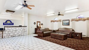 Um hall de hotel com uma mesa de recepção de pedra, sofás de couro, uma mesa de centro e ventiladores de teto.
