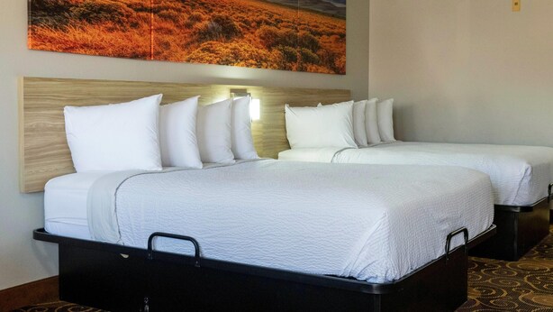 Quarto de hotel com duas camas, uma pintura grande na parede e uma cabeceira de madeira.
