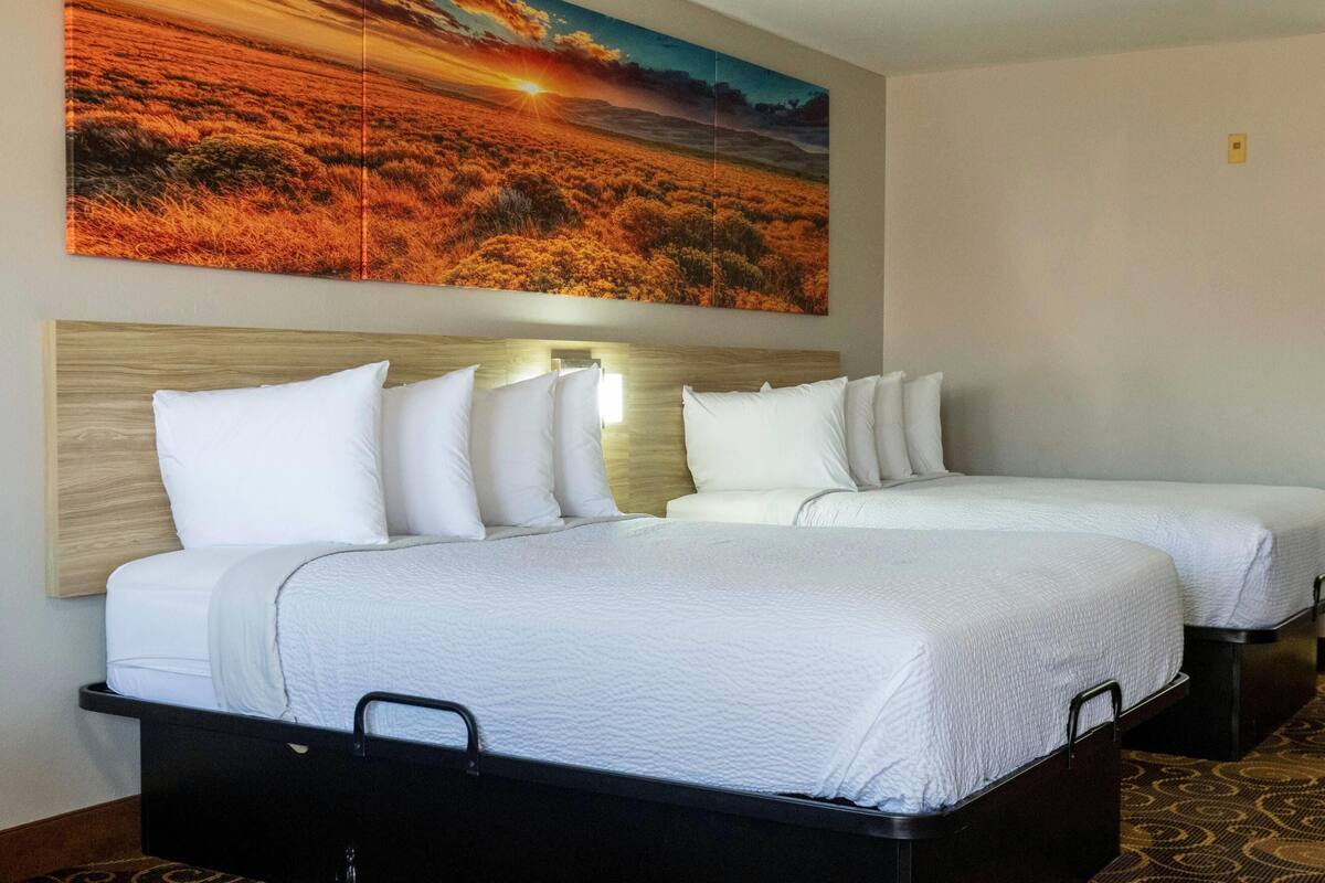 Quarto de hotel com duas camas, uma pintura grande na parede e uma cabeceira de madeira.