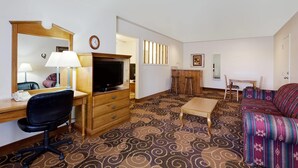 Quarto de hotel com escrivaninha, televisão, carpete estampado, sofá e pequena área de refeições.