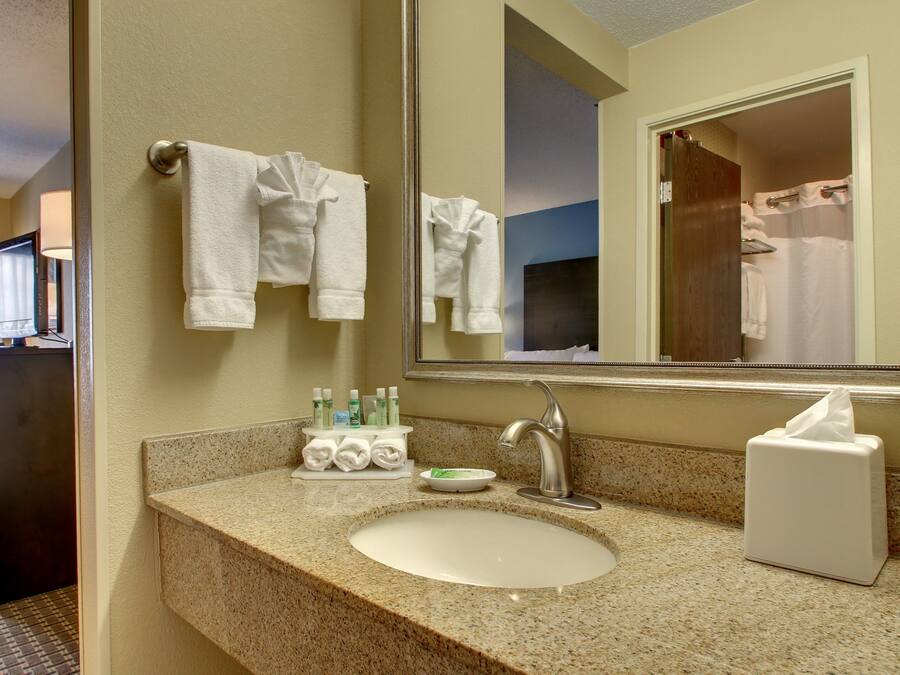 Casa de banho de hotel com lavatório, espelho, porta-toalhas e artigos de higiene pessoal.