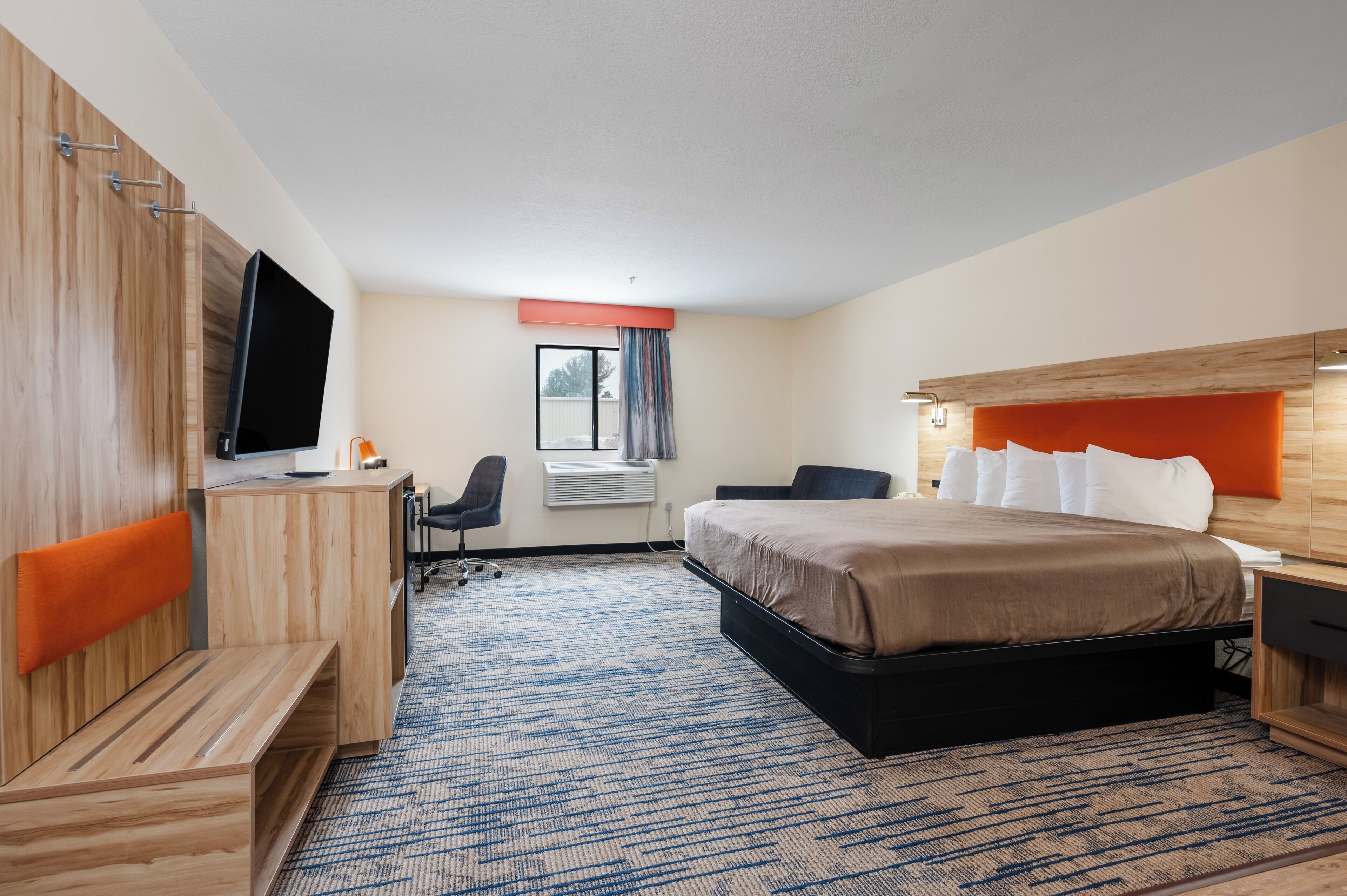 Quarto de hotel com cama, escrivaninha, cadeira, televisão e janela.