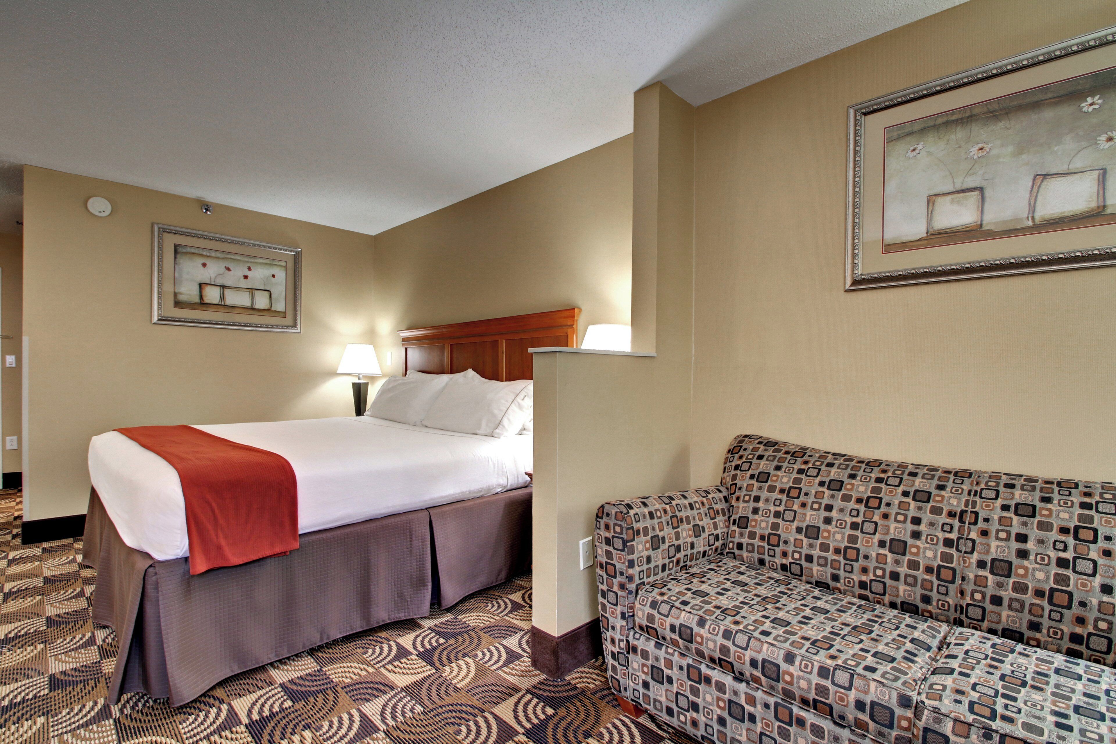 Quarto de hotel com uma cama, um sofá, um carpete estampado e duas luminárias fixadas na parede.