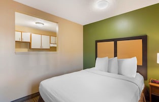 Quarto de hotel com cama, mesa de cabeceira, espelho e uma parede verde de destaque.