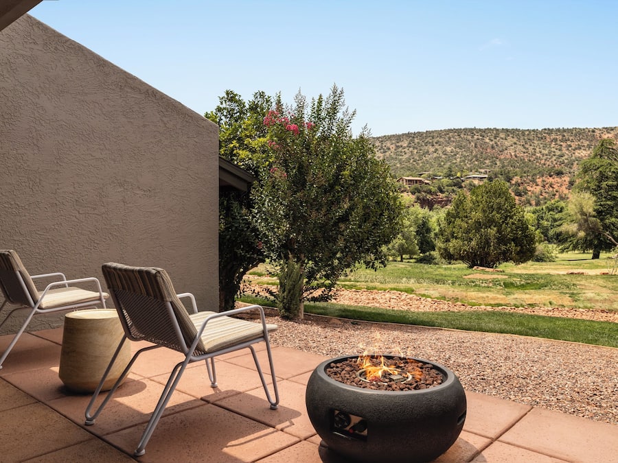Um pátio externo com duas cadeiras e uma lareira, com vista para um jardim bem cuidado e uma paisagem montanhosa.