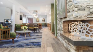 Um lobby de hotel moderno com parede em pedra decorativa, lareira e área de refeições com mobiliário de madeira.