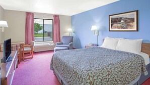 Quarto de hotel com uma cama grande, uma escrivaninha com computador, uma cadeira, janela com cortinas e um quadro na parede.