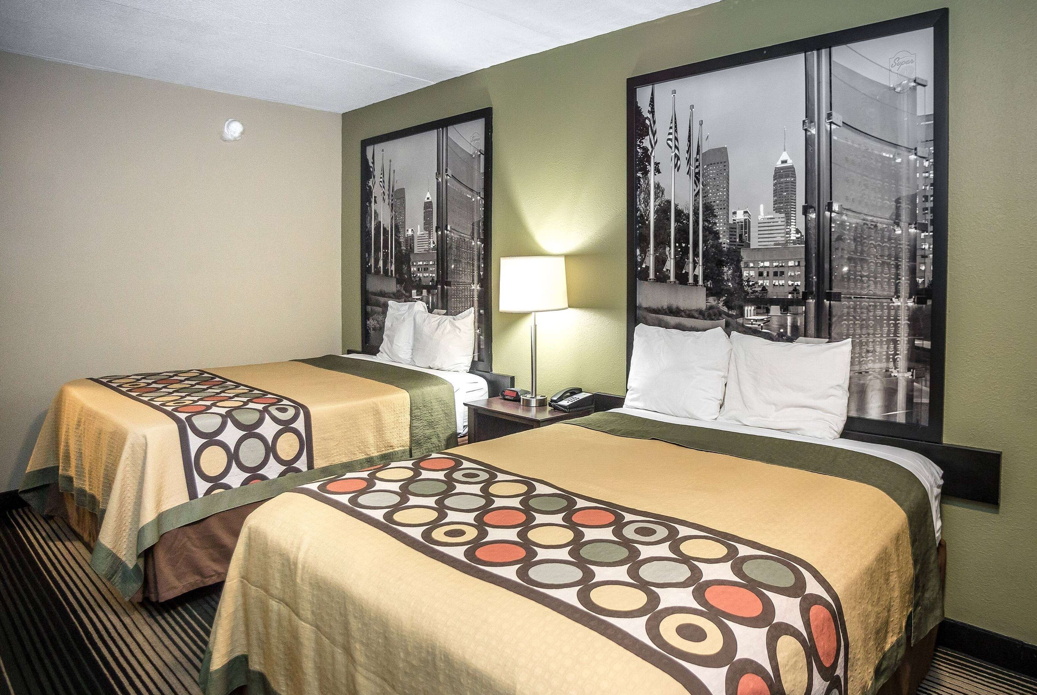 Quarto de hotel com duas camas, vista para a cidade, uma luminária e uma mesinha de cabeceira.