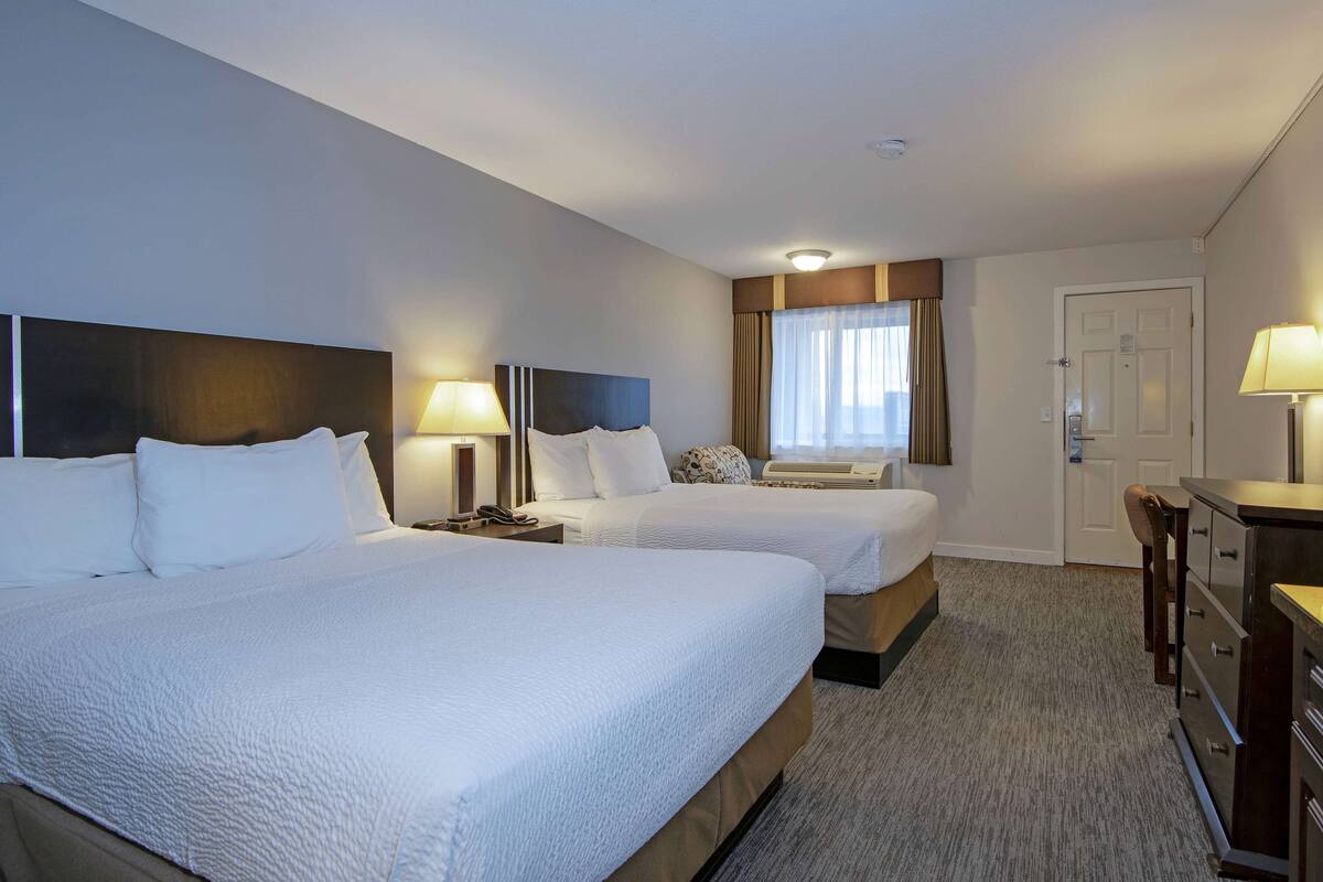 Quarto de hotel com duas camas, uma mesa, uma cadeira e uma janela com cortinas.