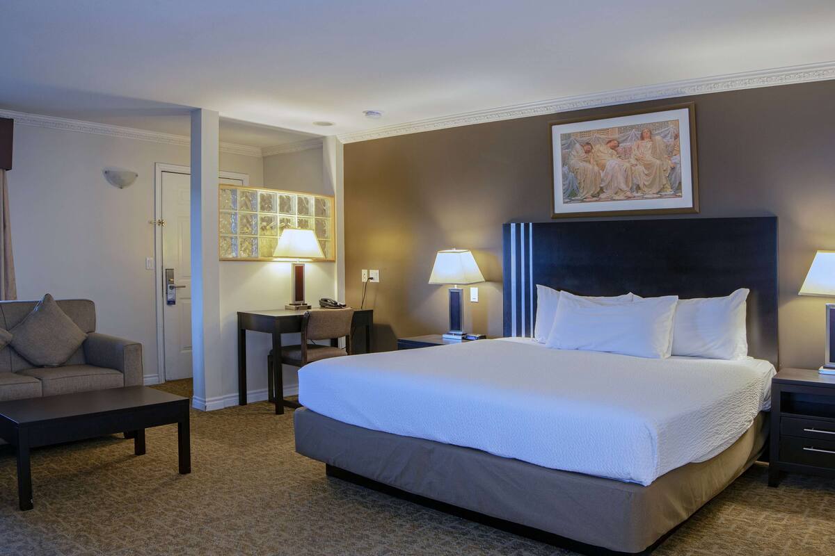 Quarto de hotel com uma cama grande, uma escrivaninha, uma cadeira e duas luminárias.