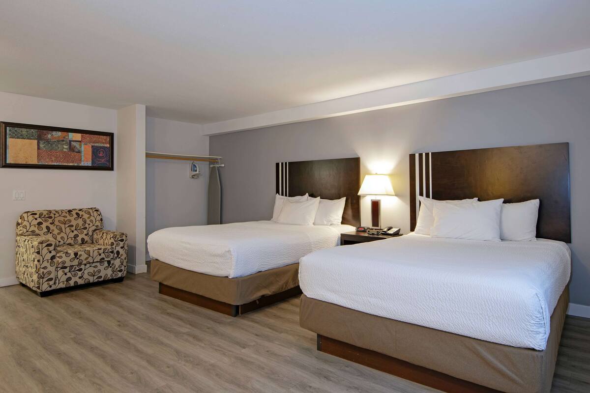 Quarto de hotel com duas camas, um sofá, um quadro na parede e um abajur.