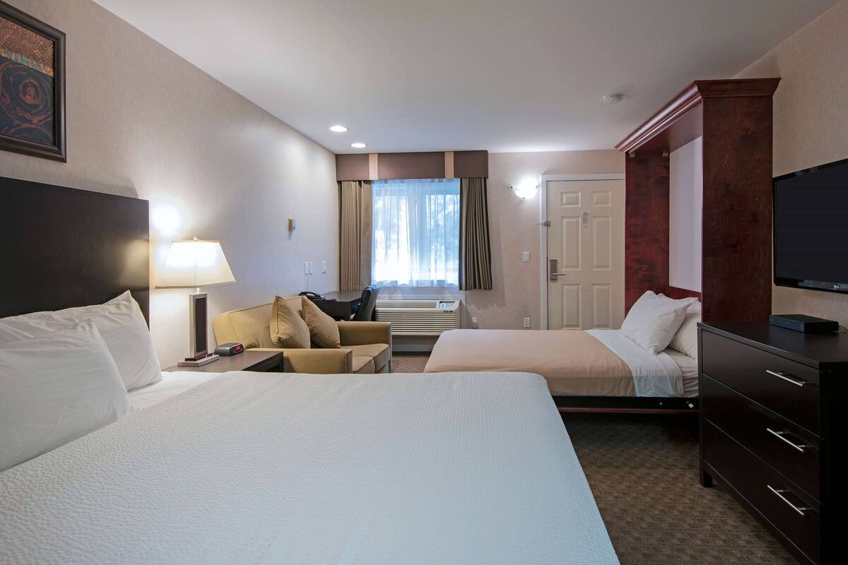 Quarto de hotel com duas camas, uma escrivaninha com luminária, uma cadeira, televisão e uma porta.