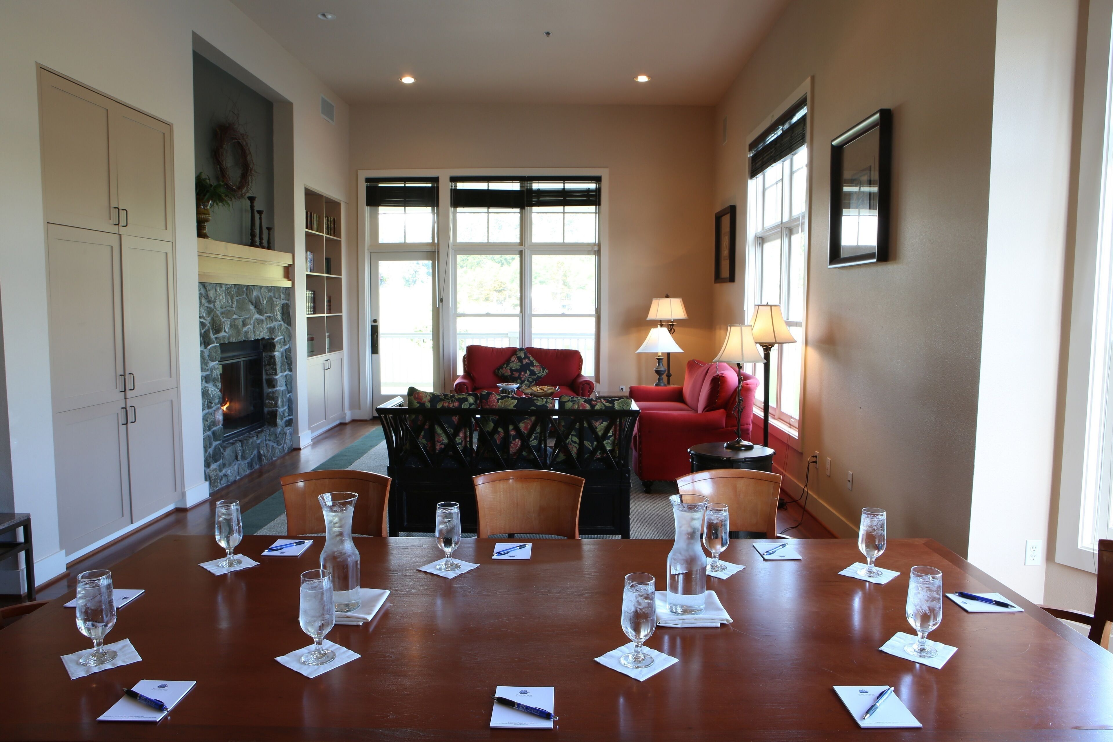 Uma sala de jantar com mesa de madeira posta para refeição, lareira e um sofá vermelho ao fundo.