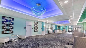Um hall amplo com carpete estampado, assentos modernos e um teto iluminado em azul.