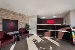 Uma área de recepção de hotel com o letreiro Red Roof Inn, uma placa indicando 'Wi-Fi Gratuito em Todas as Quartas' e uma planta.