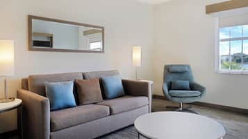 Quarto de hotel com sofá, uma cadeira, uma mesinha e janela com vista.