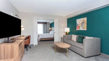 Quarto de hotel com cama, escrivaninha com computador, sofá e televisão.