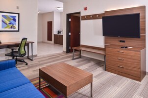Quarto de hotel moderno com televisão de tela plana, mobiliário de madeira, escrivaninha e tapete colorido.