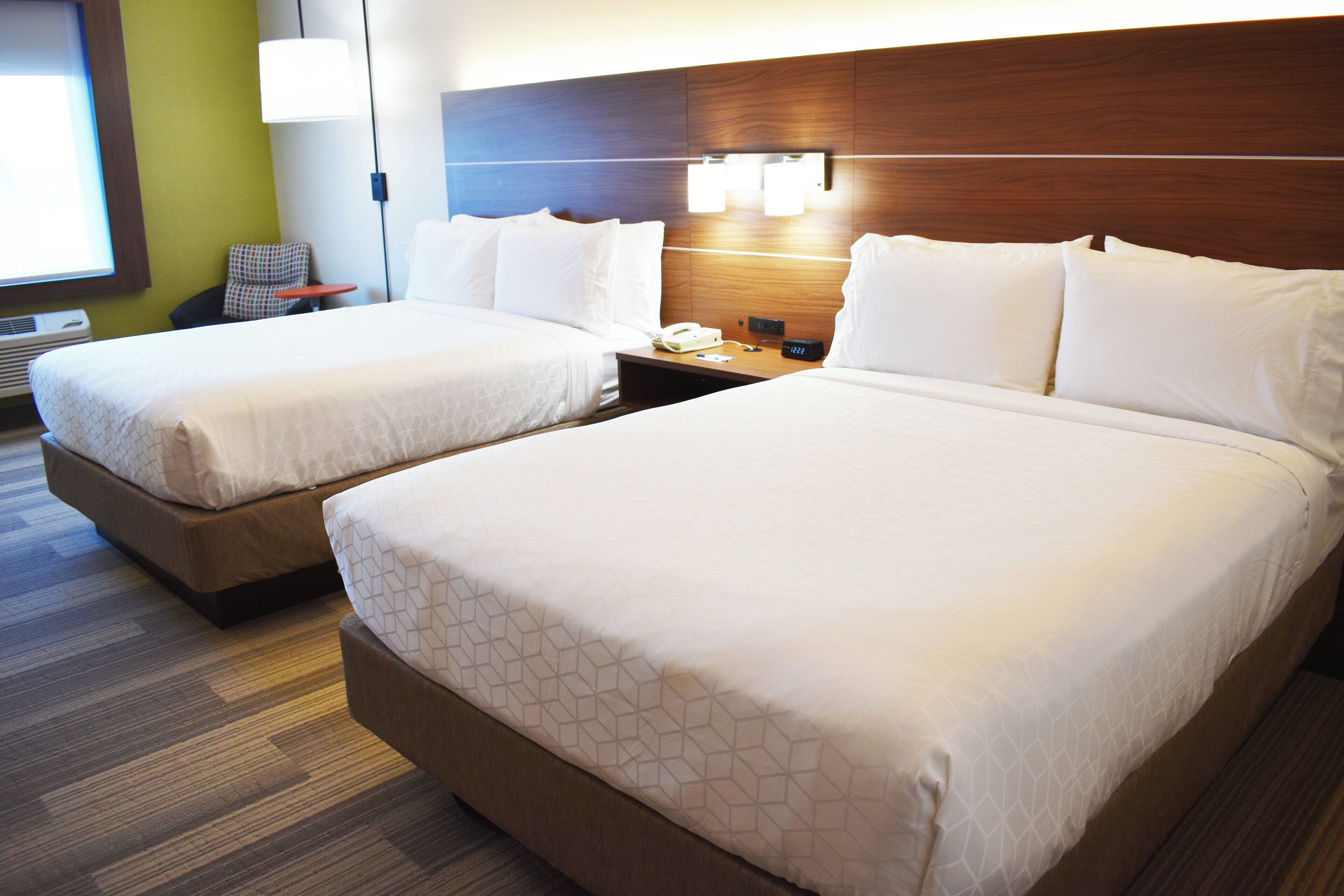 Quarto de hotel com duas camas, uma mesa de cabeceira, uma luminária e uma cadeira.