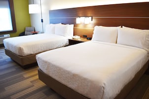 Quarto de hotel com duas camas, uma mesa de cabeceira, uma cadeira e uma luminária.