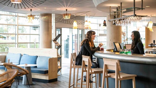 Uma área de bar moderna com banquetas de madeira, um balcão e um espaço de estar com sofá e cadeiras.