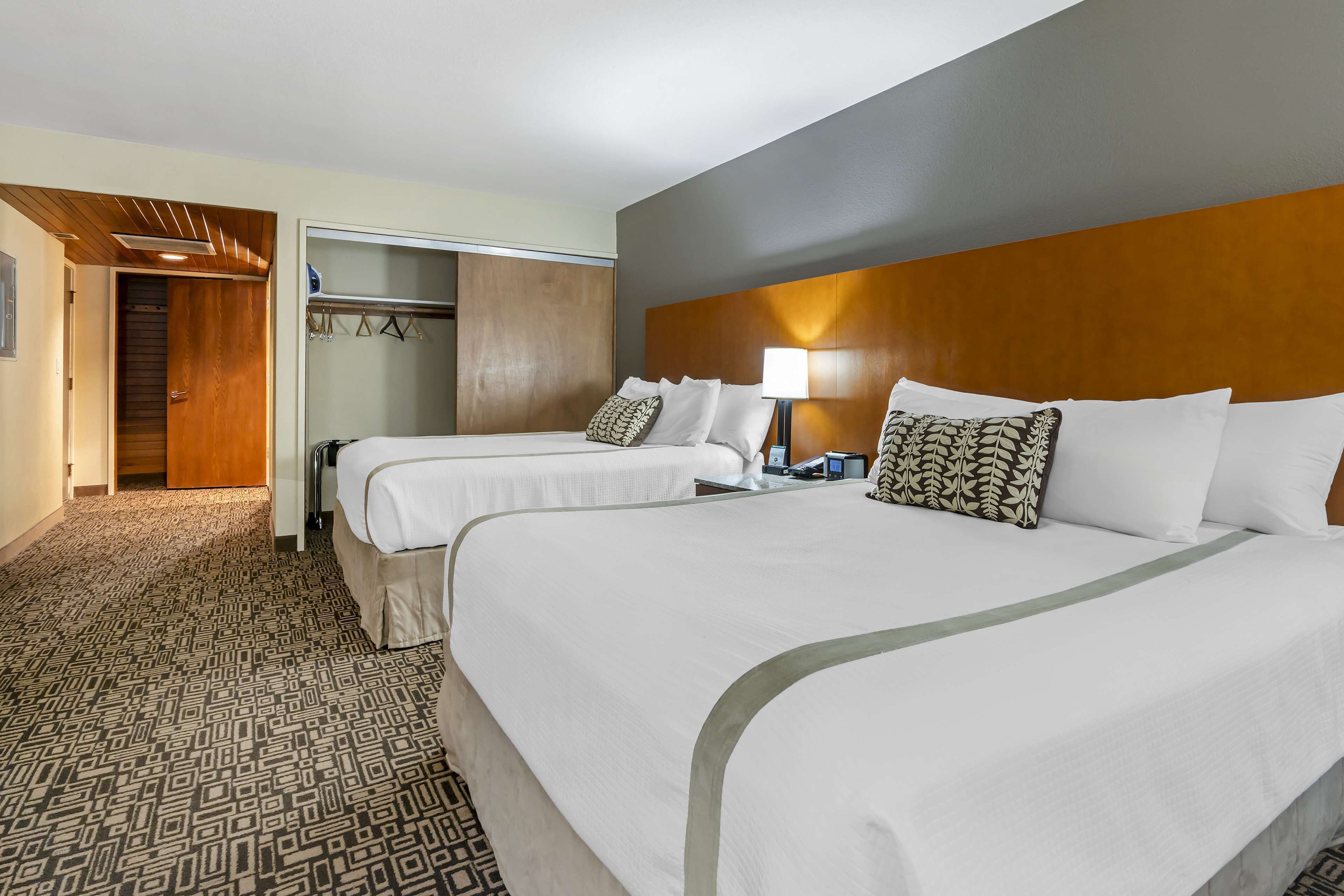 Quarto de hotel com duas camas, um closet espaçoso e um tapete estampado.
