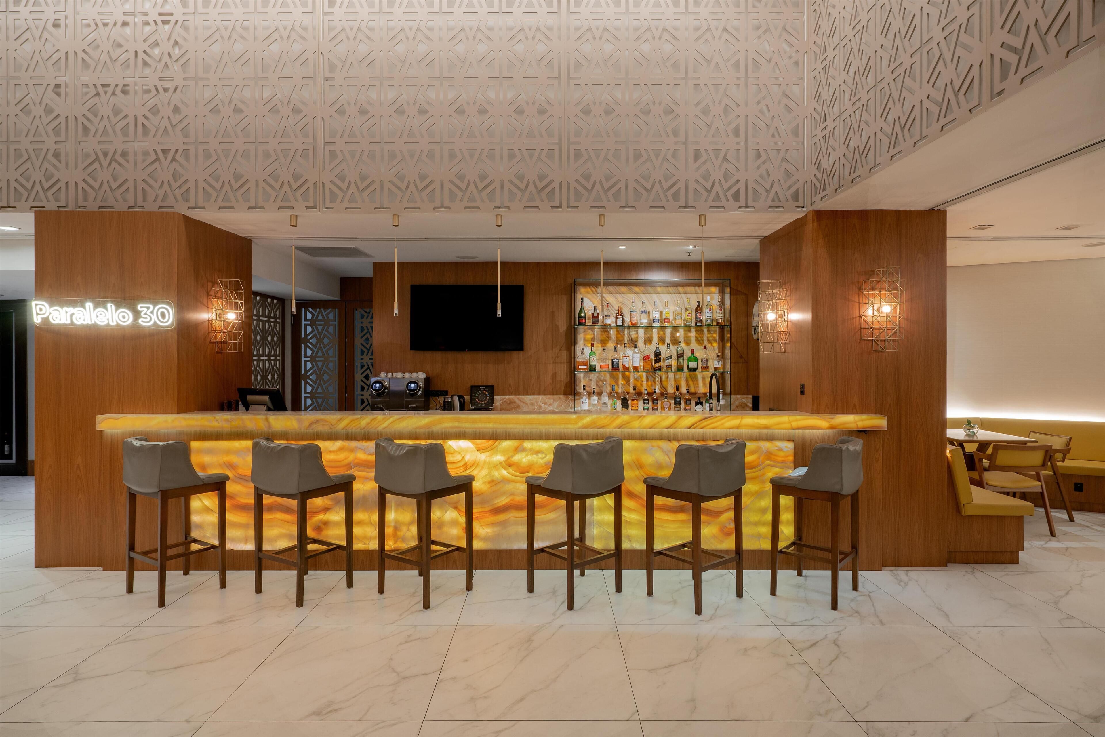Uma área de bar com piso de mármore, balcão de madeira e banquetas.
