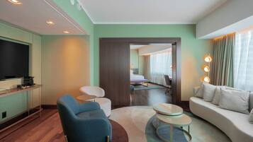 Quarto de hotel moderno com sofá, duas poltronas, uma mesinha de centro, televisão e cozinha compacta.