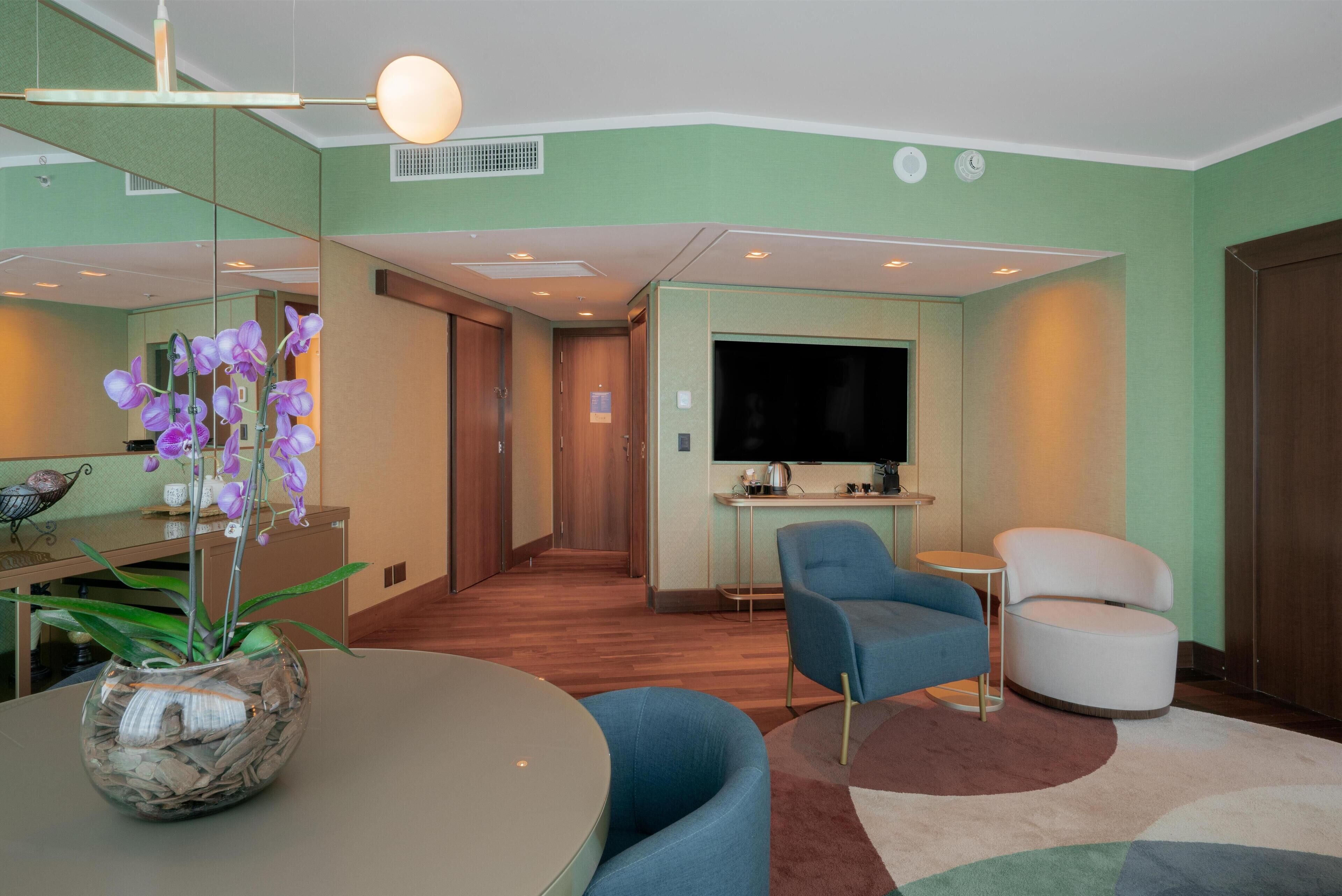 Quarto de hotel moderno com área de jantar, televisão de tela plana e um espelho grande.