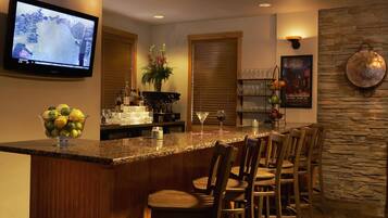 Uma área de bar com bancada de granito, banquetas, televisão, planta em vaso e adega.