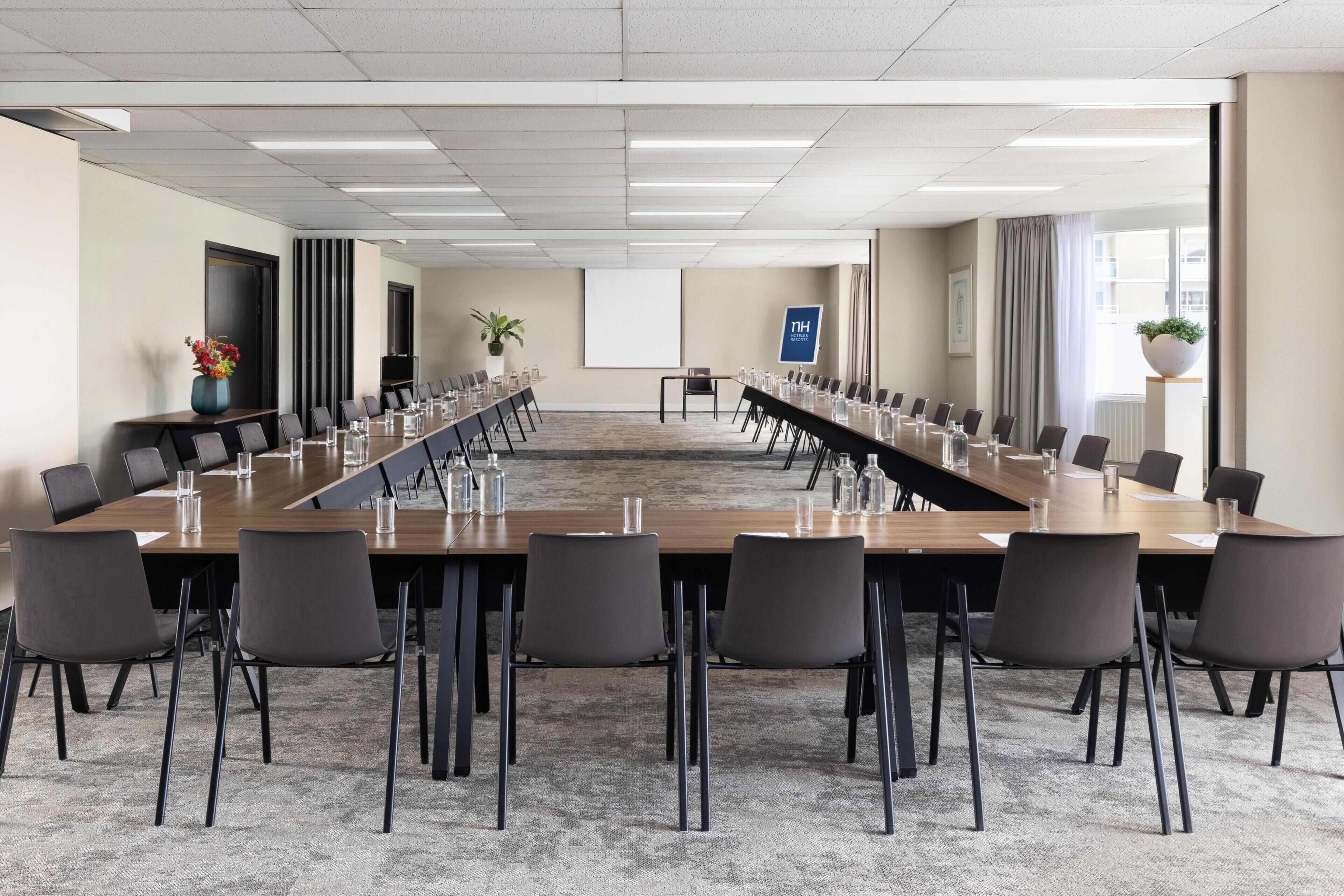 Uma sala de conferências com uma mesa comprida, cadeiras, uma tela de projetor e um logotipo na parede.