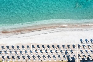 Vista aérea de uma praia com uma fileira de guarda-sóis alinhados e uma orla arenosa.
