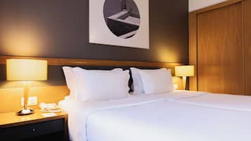 Quarto de hotel com uma cama, duas luminárias de cabeceira, mesa de cabeceira com telefone e um quadro na parede.