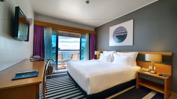 Quarto de hotel com cama, mesa de cabeceira, abajur e vista para o exterior.