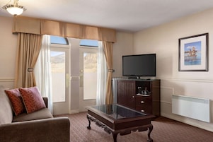 Quarto de hotel com sofá, mesa de centro de vidro, TV em um armário, quadro na parede e vista do deserto pela janela.
