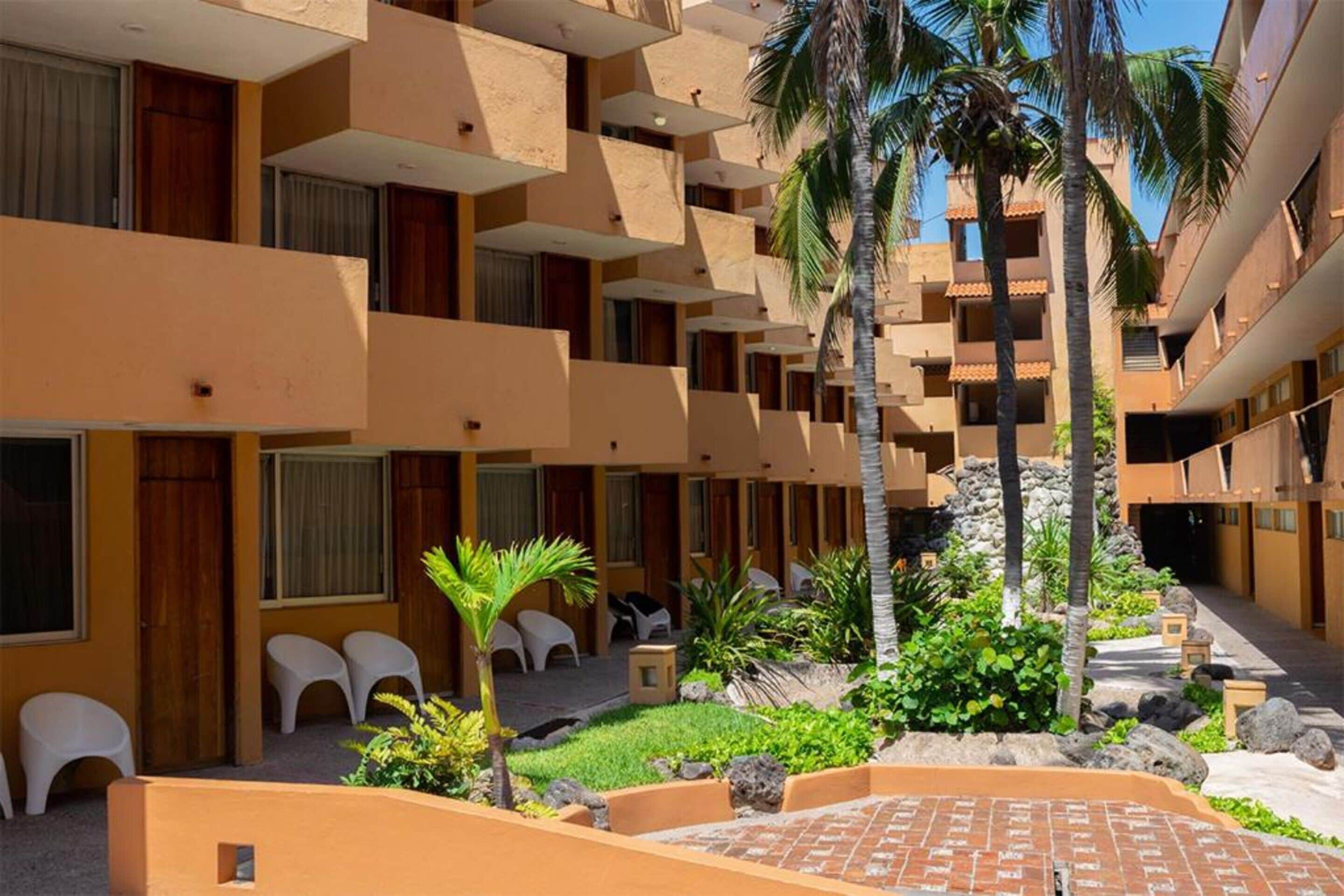 Pátio de hotel com várias varandas, palmeiras e áreas de estar ao ar livre.