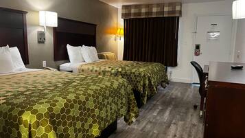 Quarto de hotel com duas camas, uma escrivaninha, uma cadeira e janela com cortinas.