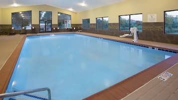 Piscina com elevador de piscina, cadeiras de descanso e vista para o exterior através de grandes janelas.