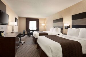 Quarto de hotel com duas camas, uma escrivaninha, uma cadeira, uma televisão e uma janela com cortinas.