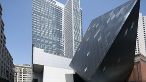 Um edifício moderno com um design angular único, rodeado por outros edifícios altos.