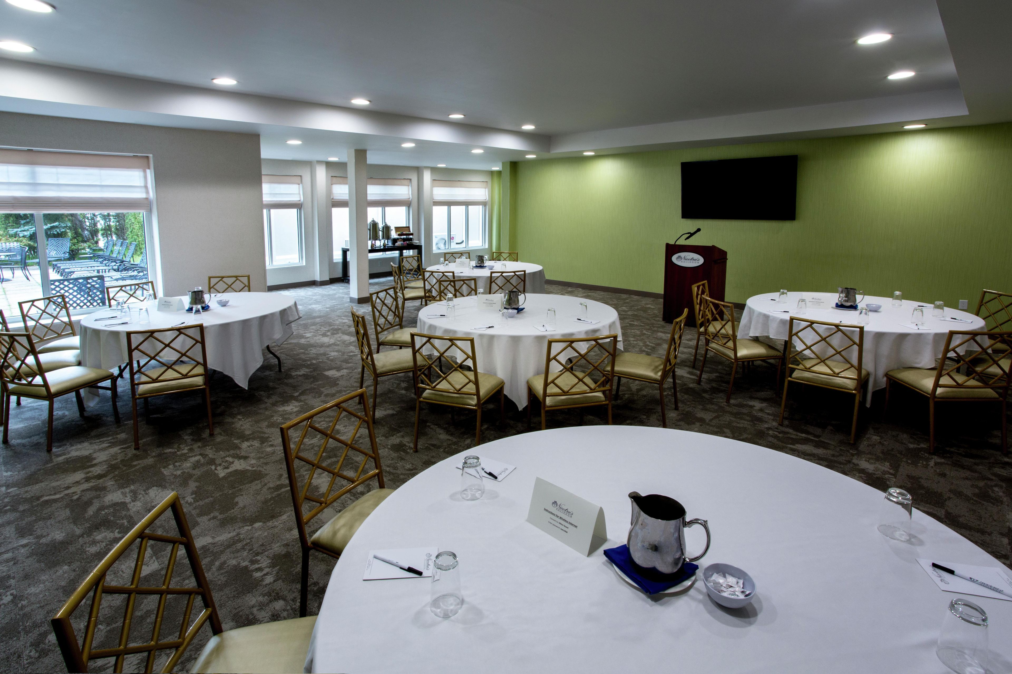 Sala de conferências com várias mesas redondas, cadeiras e um pódio.