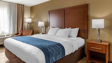 Quarto de hotel com uma cama grande, duas luminárias de cabeceira, uma cadeira e uma mesinha de cabeceira.
