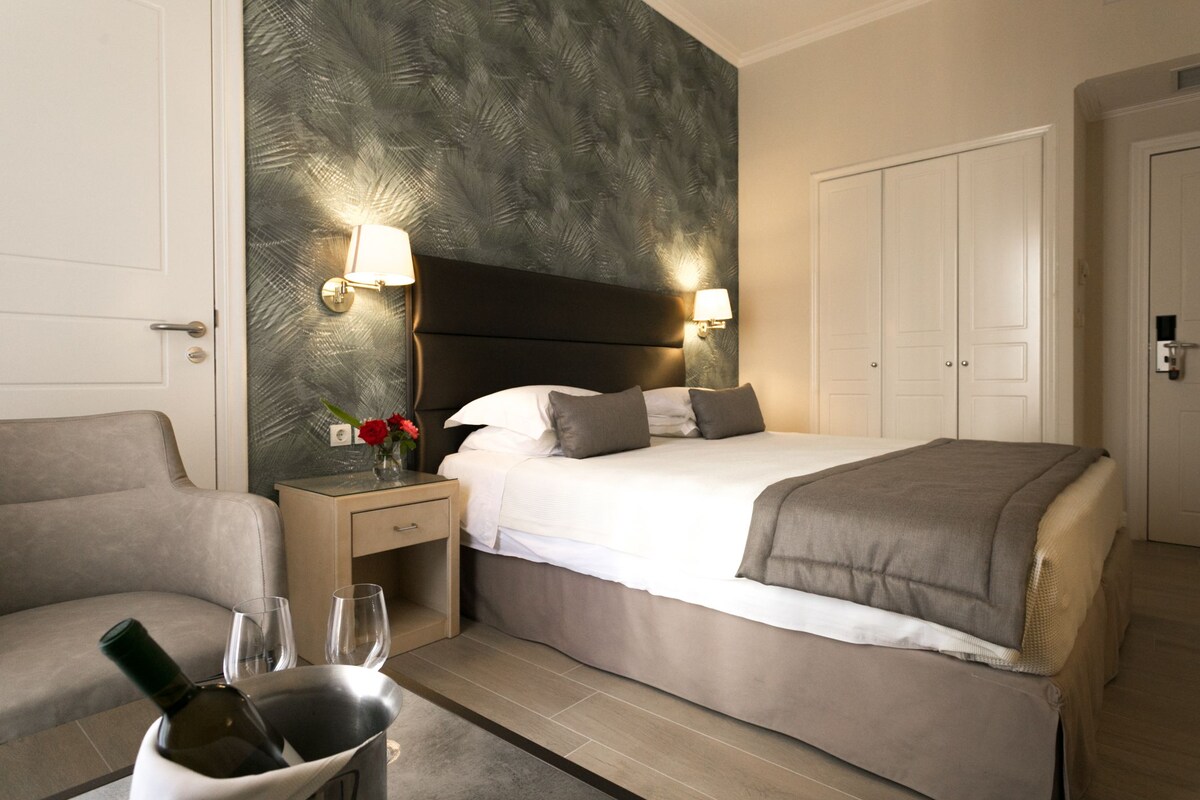 Quarto de hotel com cama, mesas de cabeceira, uma cadeira e uma garrafa de vinho.