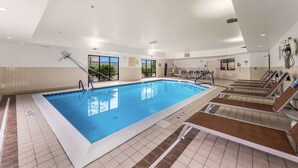 Piscina com água azul cristalina, rodeada por espreguiçadeiras e um chão de azulejos.