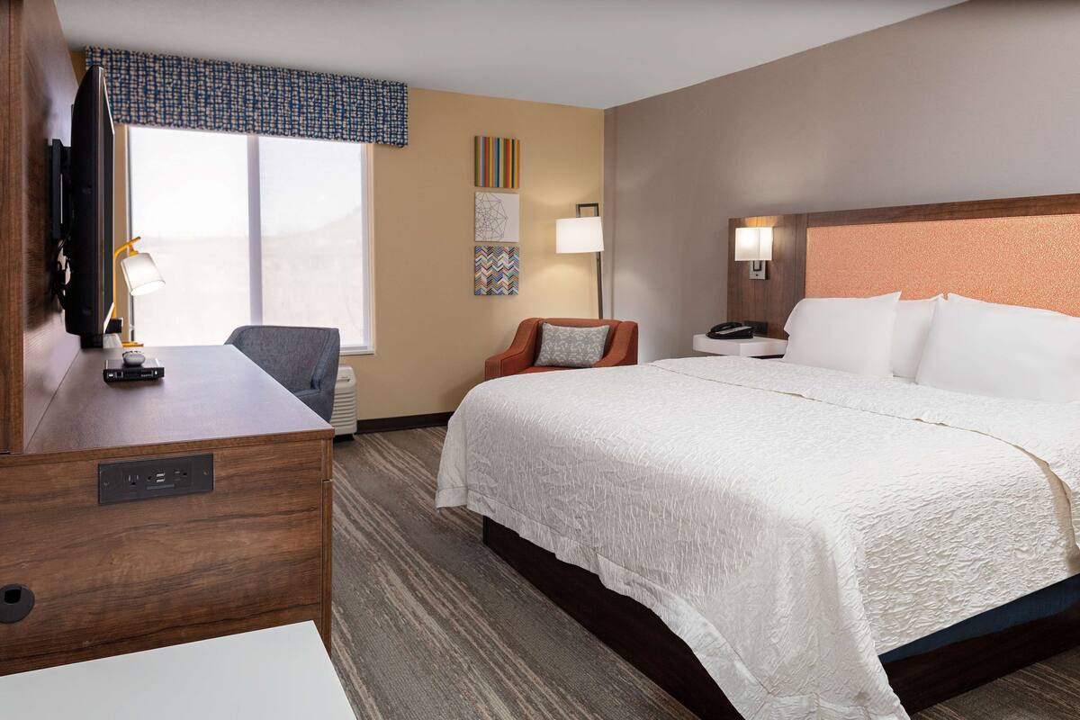Quarto de hotel com cama, escrivaninha, cadeira, televisão e janela com vista.