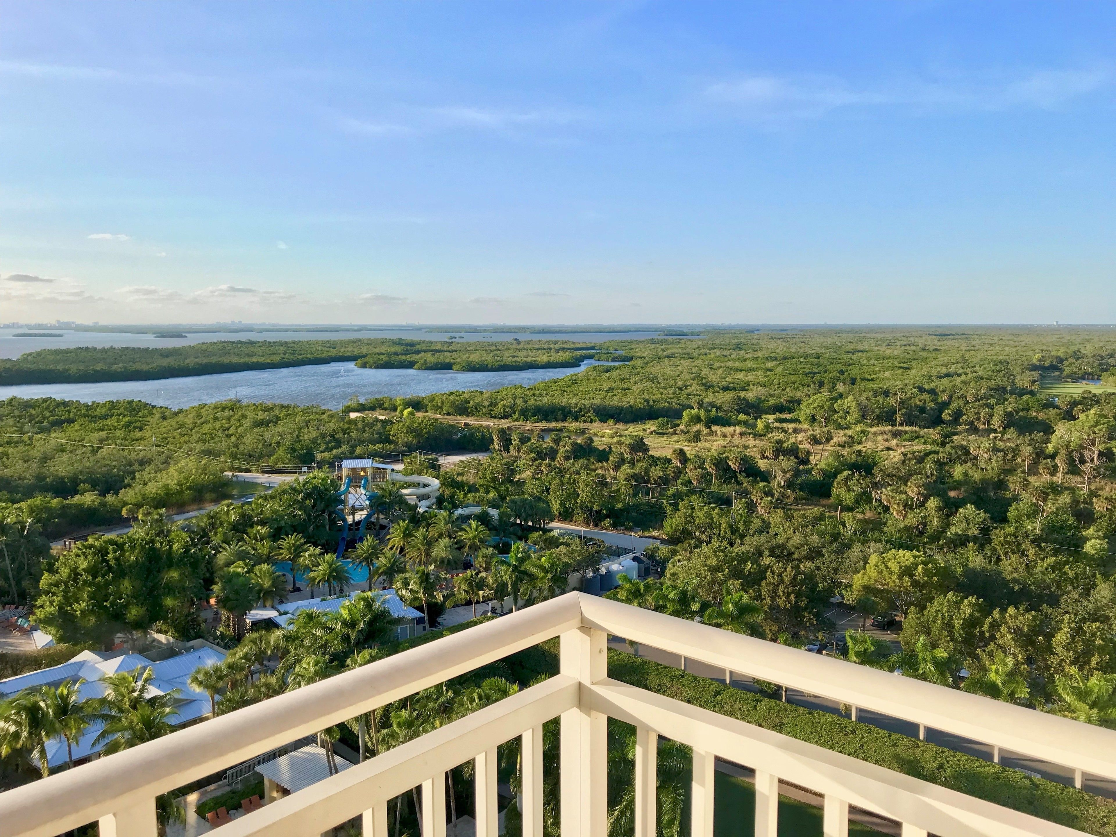 Vista de uma varanda com paisagem exuberante, com um corpo d'água, vegetação densa e o horizonte distante da cidade.
