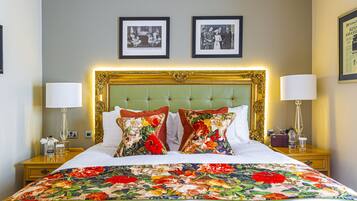 Cama bem arrumada com colcha florida, cabeceira estofada verde e duas fotografias emolduradas na parede acima.