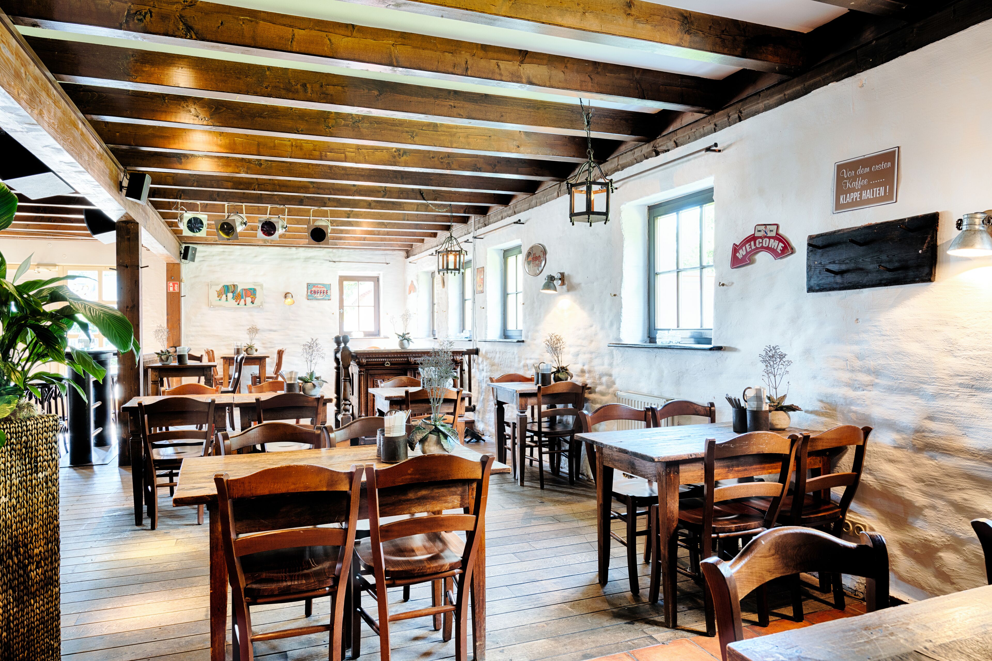 Um interior rústico com mesas e cadeiras de madeira, vigas aparentes e uma placa acolhedora.